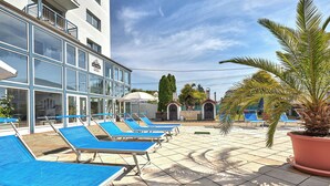 Uma área à beira da piscina com espreguiçadeiras azuis, uma palmeira e um edifício com uma placa.