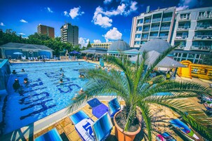 Uma piscina com espreguiçadeiras e guarda-sóis, cercada por edifícios e palmeiras.
