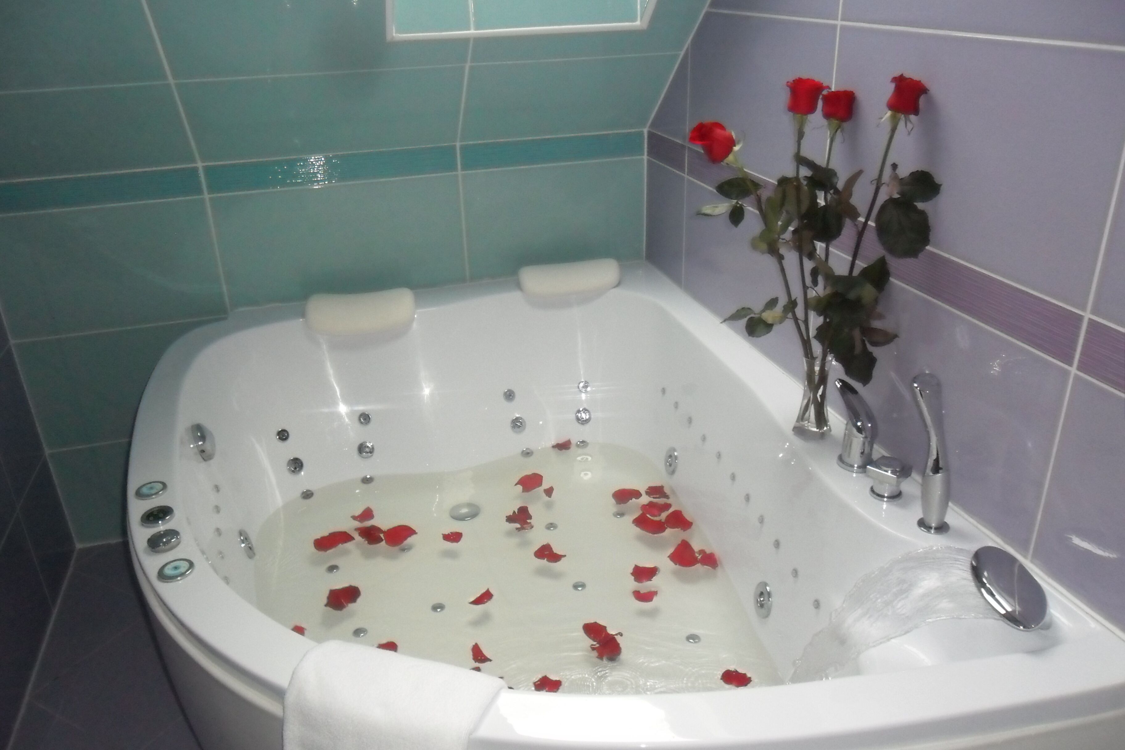 Uma banheira com pétalas de rosa, uma toalha branca e raminhos de rosa.