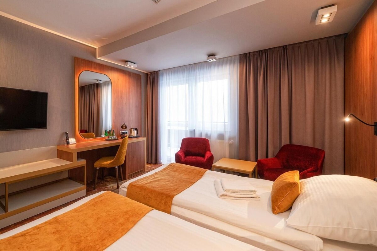 Quarto de hotel com duas camas, uma escrivaninha, uma cadeira e uma televisão.