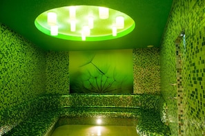 Um quarto com uma parede em mosaico verde, um lustre central e um mural de árvore.