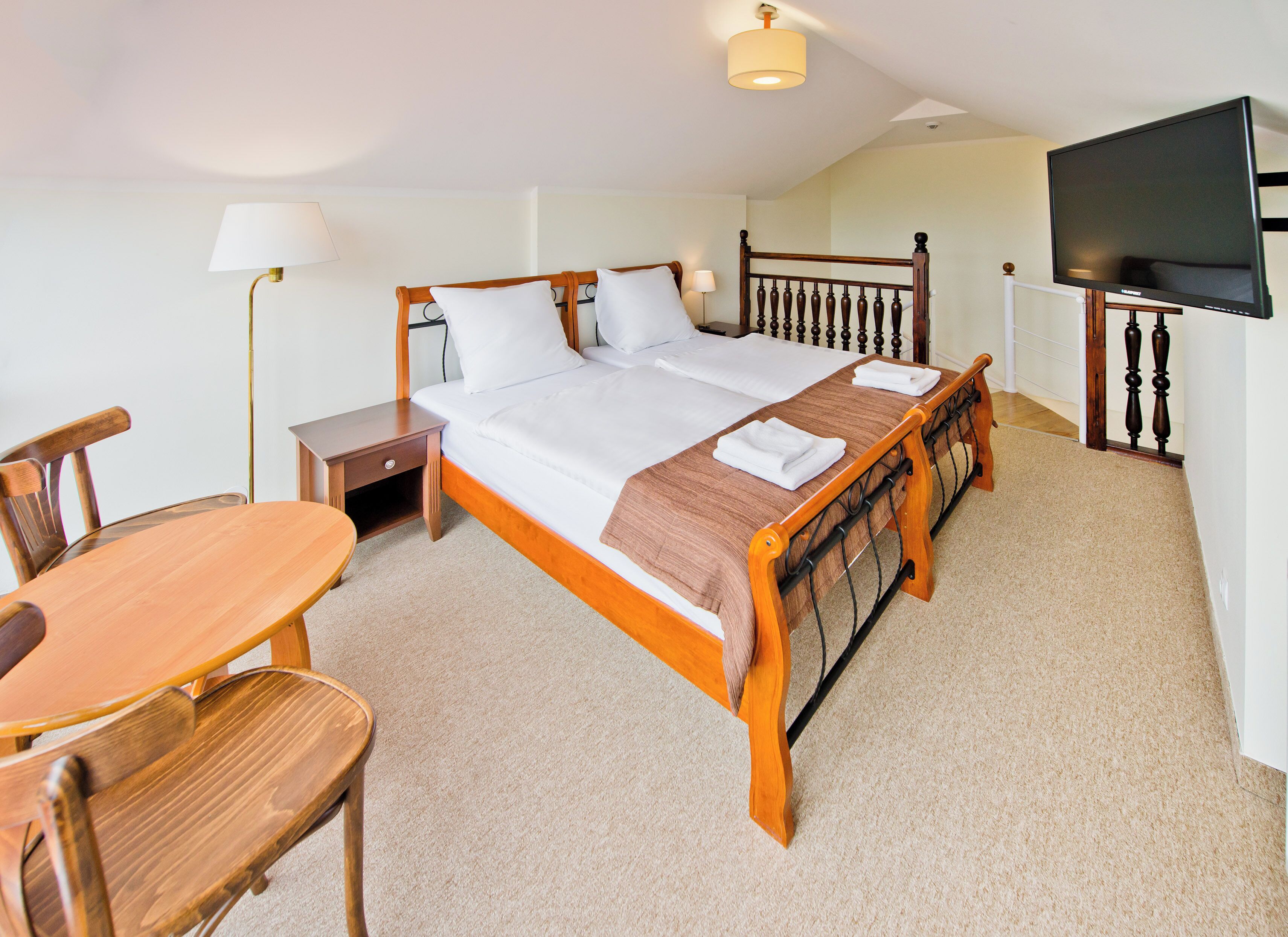 Quarto de hotel bem arrumado, com cama, mesas de cabeceira, televisão, escrivaninha e cadeira.