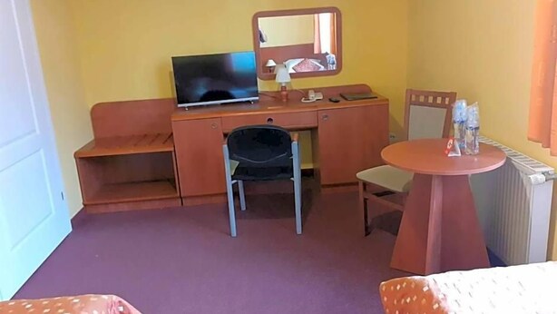 Quarto de hotel com cama, escrivaninha, cadeira, mesa redonda e radiador.