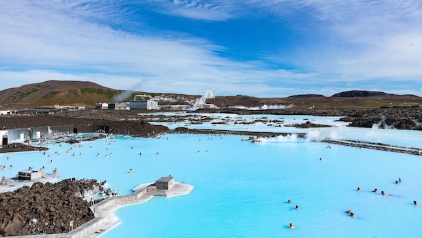 Um spa geotérmico com uma piscina grande, cercada por terreno rochoso e edifícios.
