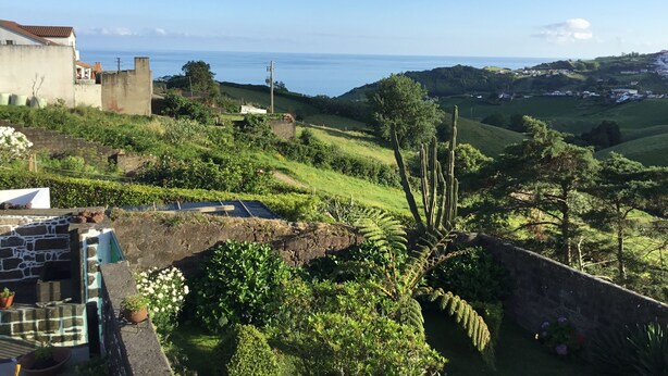 Paisagem costeira com vista para o mar, colinas verdes e um edifício com parede de pedra.