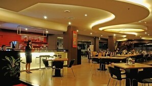 Um interior de restaurante moderno com área de bar, diversas mesas de jantar e um balcão.