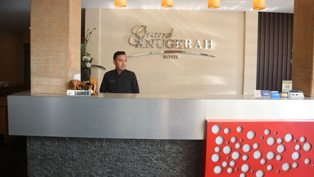 Bancada de recepção do Hotel Grand Anugerah, com uma máquina registradora, placa de identificação e máquinas de cartão de pagamento.