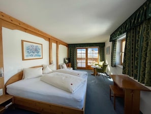 Quarto de hotel com duas camas, uma escrivaninha, uma cadeira e vista para uma paisagem nevada.