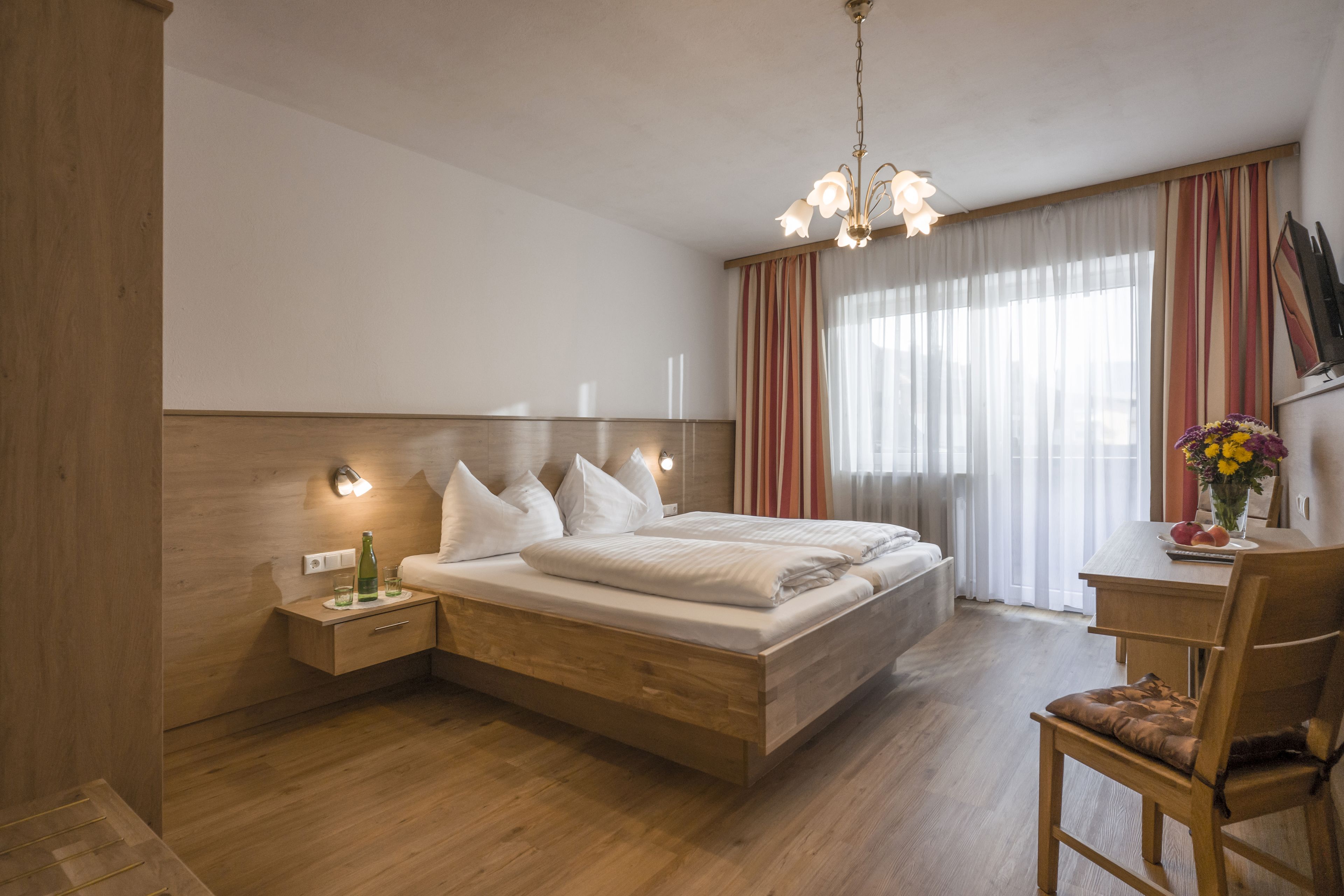 Quarto de hotel moderno com cama de madeira, mesas de cabeceira, escrivaninha e uma cadeira.