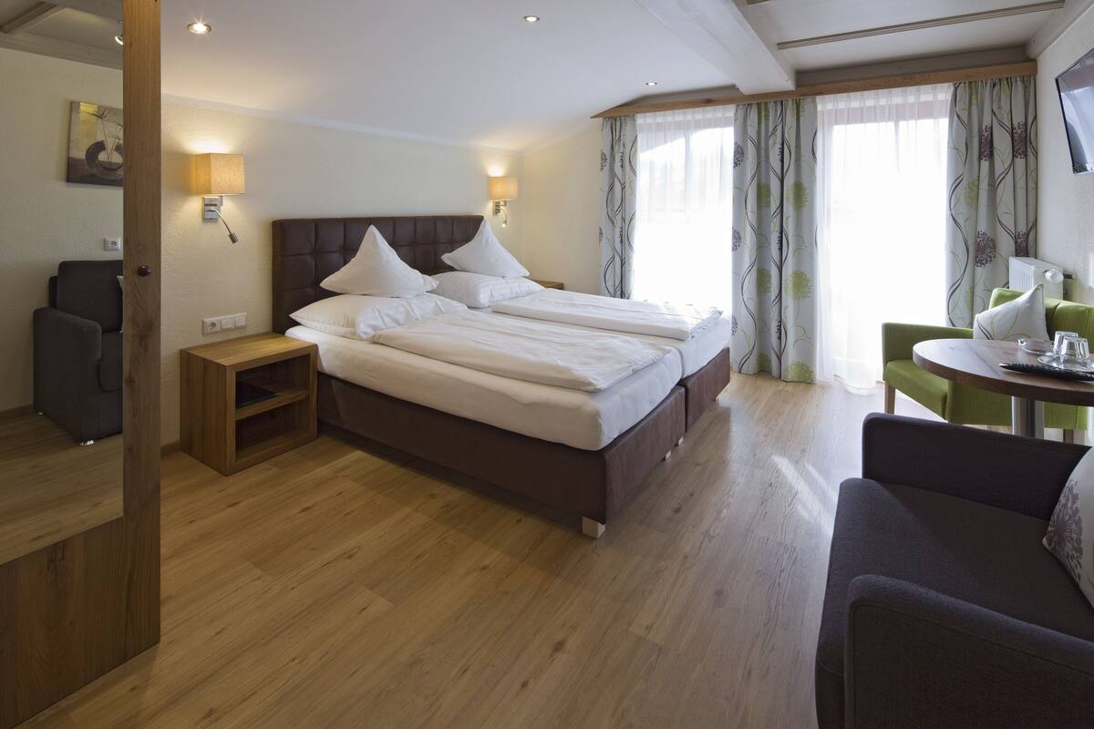 Quarto de hotel com uma cama grande, mesas de cabeceira, escrivaninha e uma cadeira.
