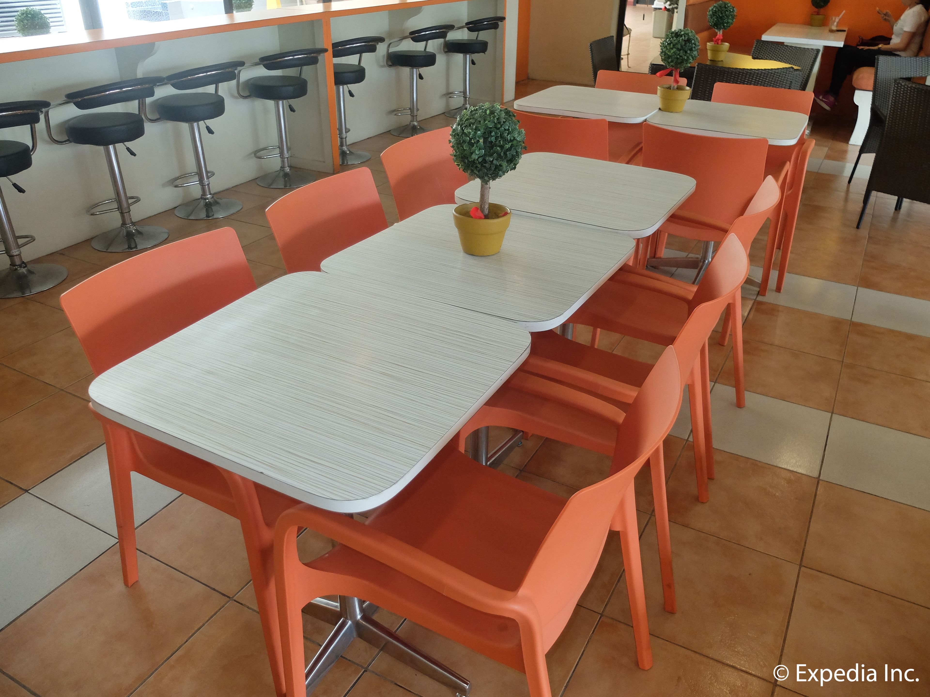 Restaurante com cadeiras e mesas laranja, área de bar com bancos e uma pequena planta em vaso sobre a mesa.