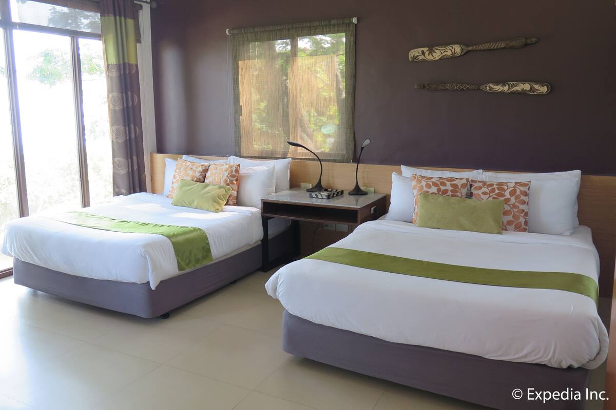 Quarto de hotel com duas camas, uma escrivaninha e uma janela com cortinas.