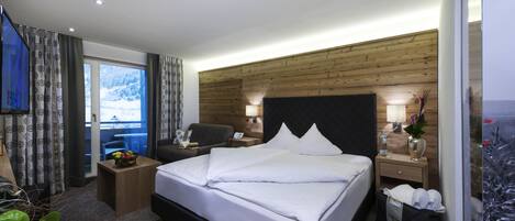 Quarto de hotel com uma cama grande, uma escrivaninha, uma cadeira e vista para as montanhas pela janela.