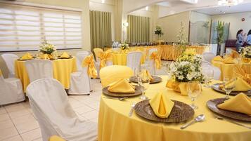 Salão de banquetes com mesas redondas cobertas por toalhas amarelas e cadeiras brancas, cada uma decorada com fitas amarelas.