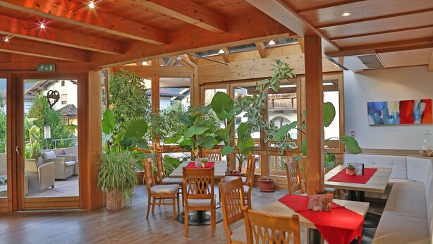 Restaurante com vigas de madeira, grandes vasos de plantas e uma combinação de áreas de refeições e assentos.