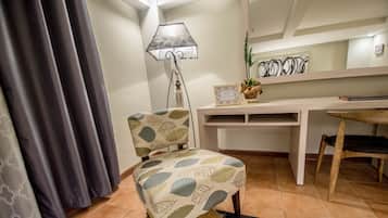 Uma sala de estar com uma poltrona estampada, uma escrivaninha, uma luminária e uma pequena planta.