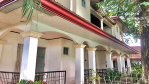 Um edifício com área externa coberta, teto vermelho, colunas brancas e varanda com guarda-corpo.