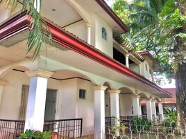 Um edifício com área externa coberta, teto vermelho, colunas brancas e varanda com guarda-corpo.
