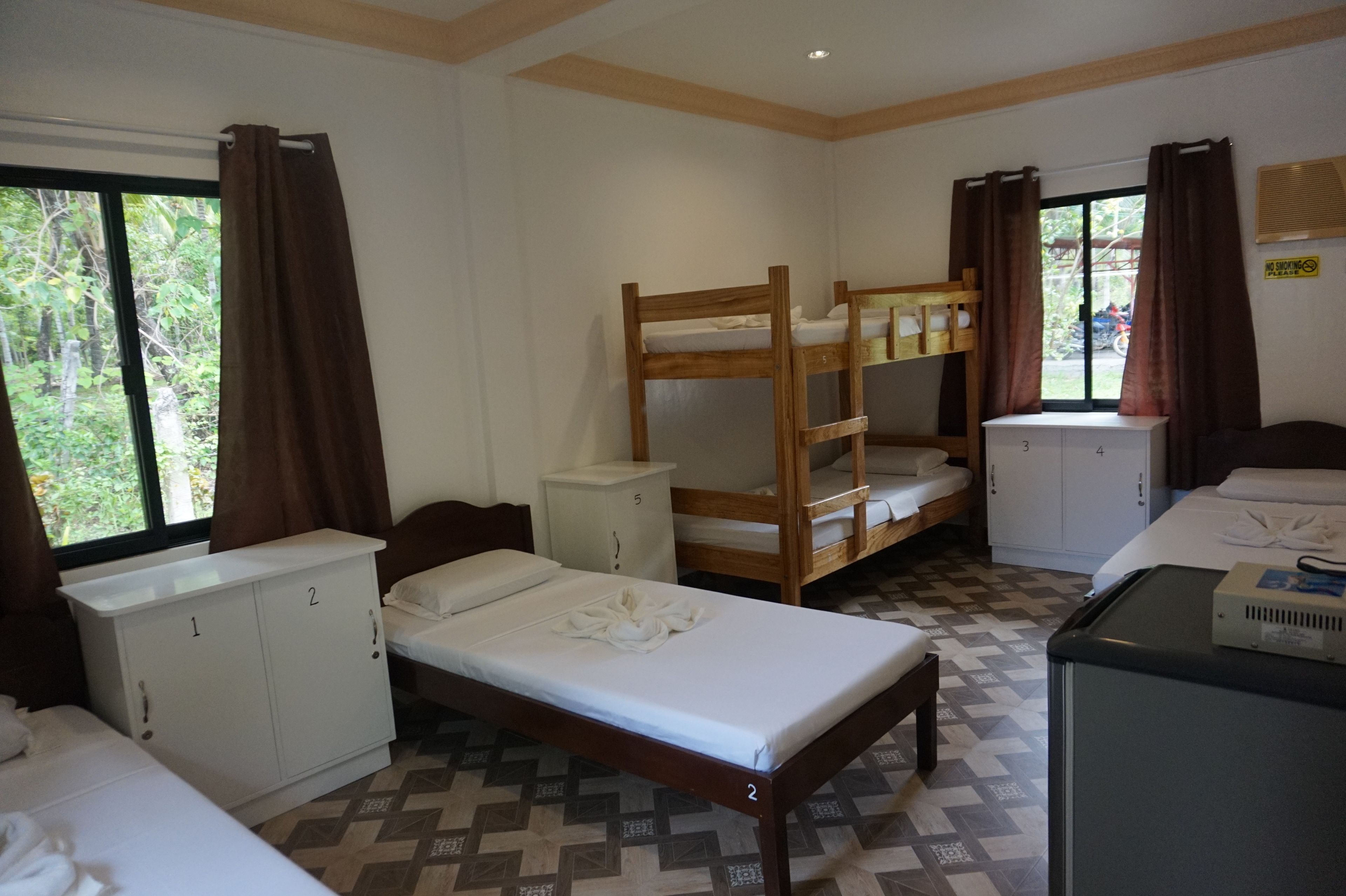 Quarto com beliches, uma escrivaninha, um armário e uma janela com cortinas.