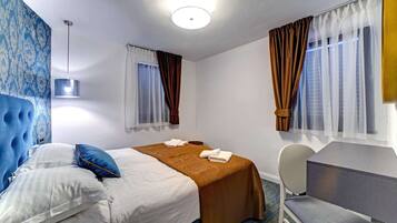 Quarto de hotel com cama, uma cadeira, escrivaninha e janela com cortinas.
