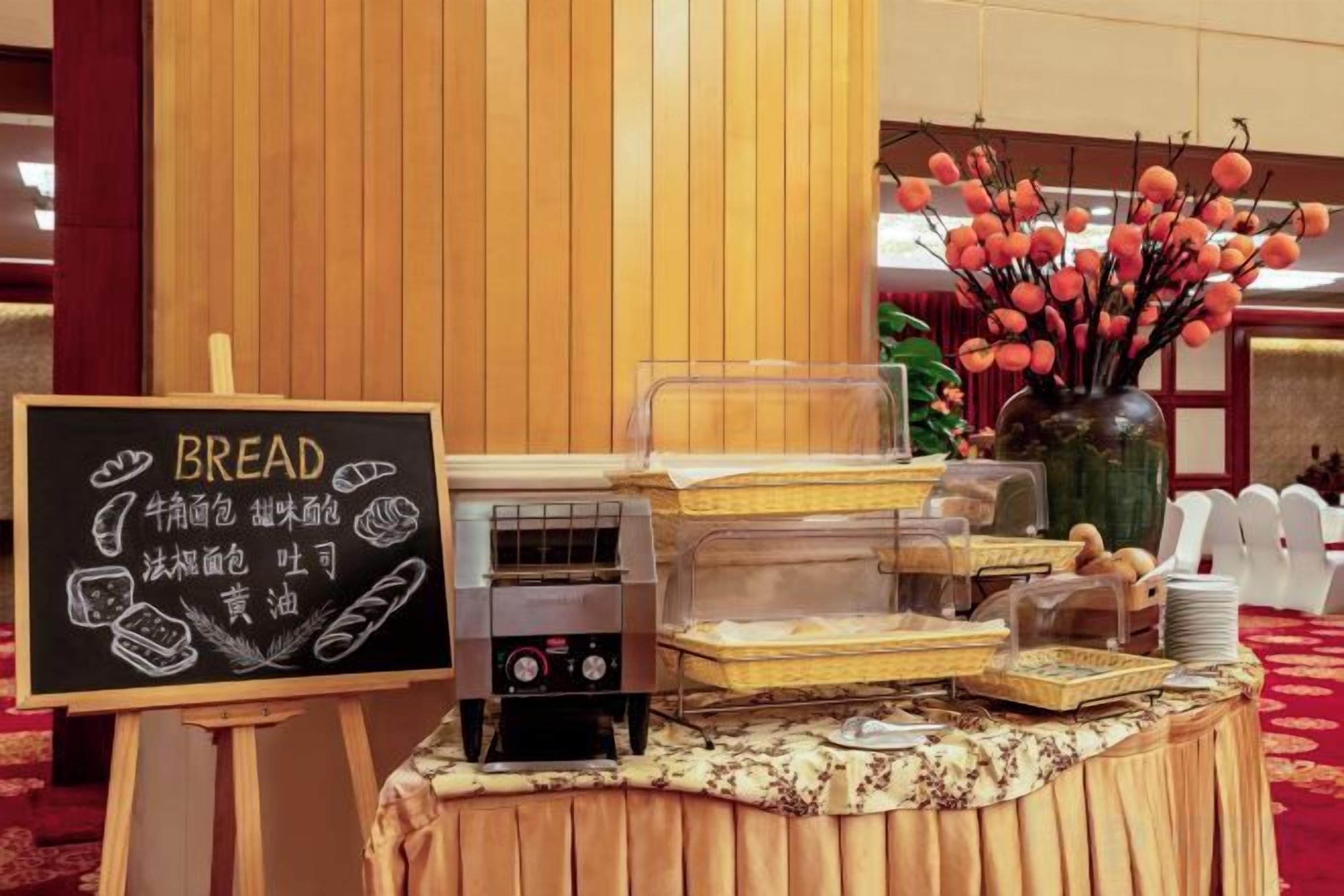 Disposição de buffet com pães, uma torradeira e diversos recipientes de comida sobre uma mesa.