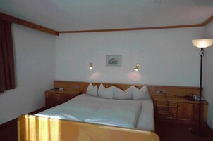 Quarto de hotel com uma cama de solteiro, cabeceira de madeira, mesas de cabeceira, um criado-mudo, um abajur e um quadro emoldurado na parede.
