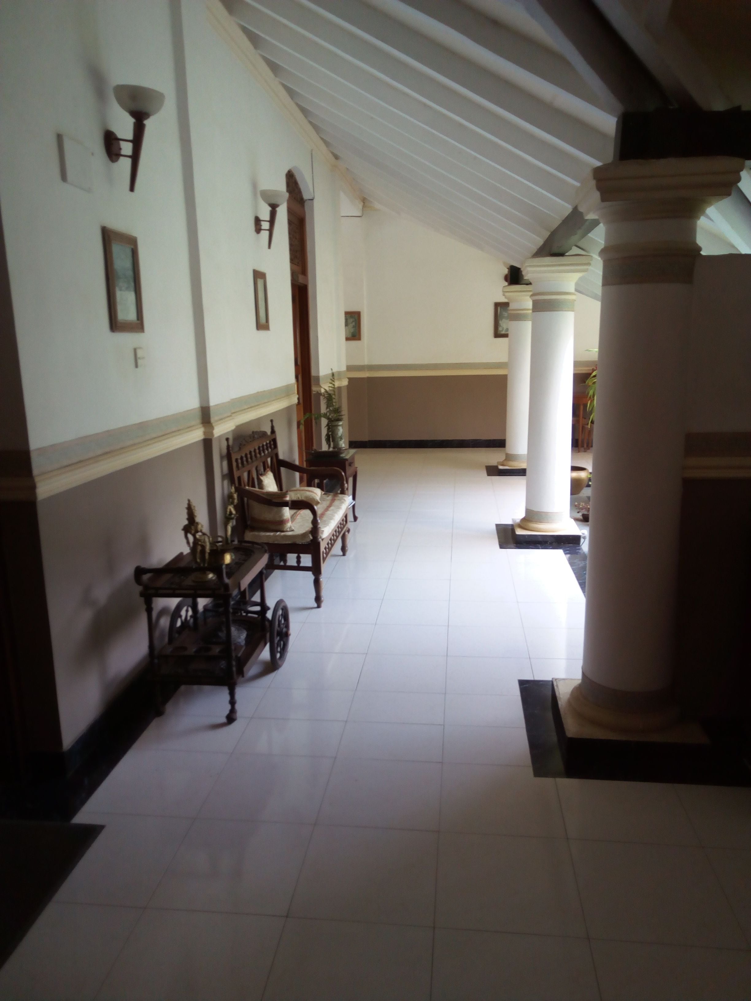 Um corredor com piso de azulejos brancos, bancos de madeira e colunas.