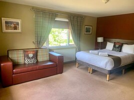 Um quarto com cama, um sofá de couro marrom, uma janela com cortinas e duas fotos emolduradas na parede.