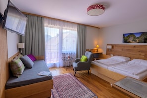 Quarto de hotel com cama, sofá, poltrona, mesinha com uma garrafa, televisão e um quadro na parede.