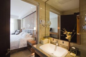 Quarto de hotel moderno com uma cama grande, banheiro com um espelho amplo e toucador com pia.