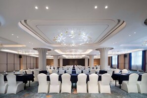 Sala de conferência com mesas redondas, cadeiras brancas e um lustre moderno.