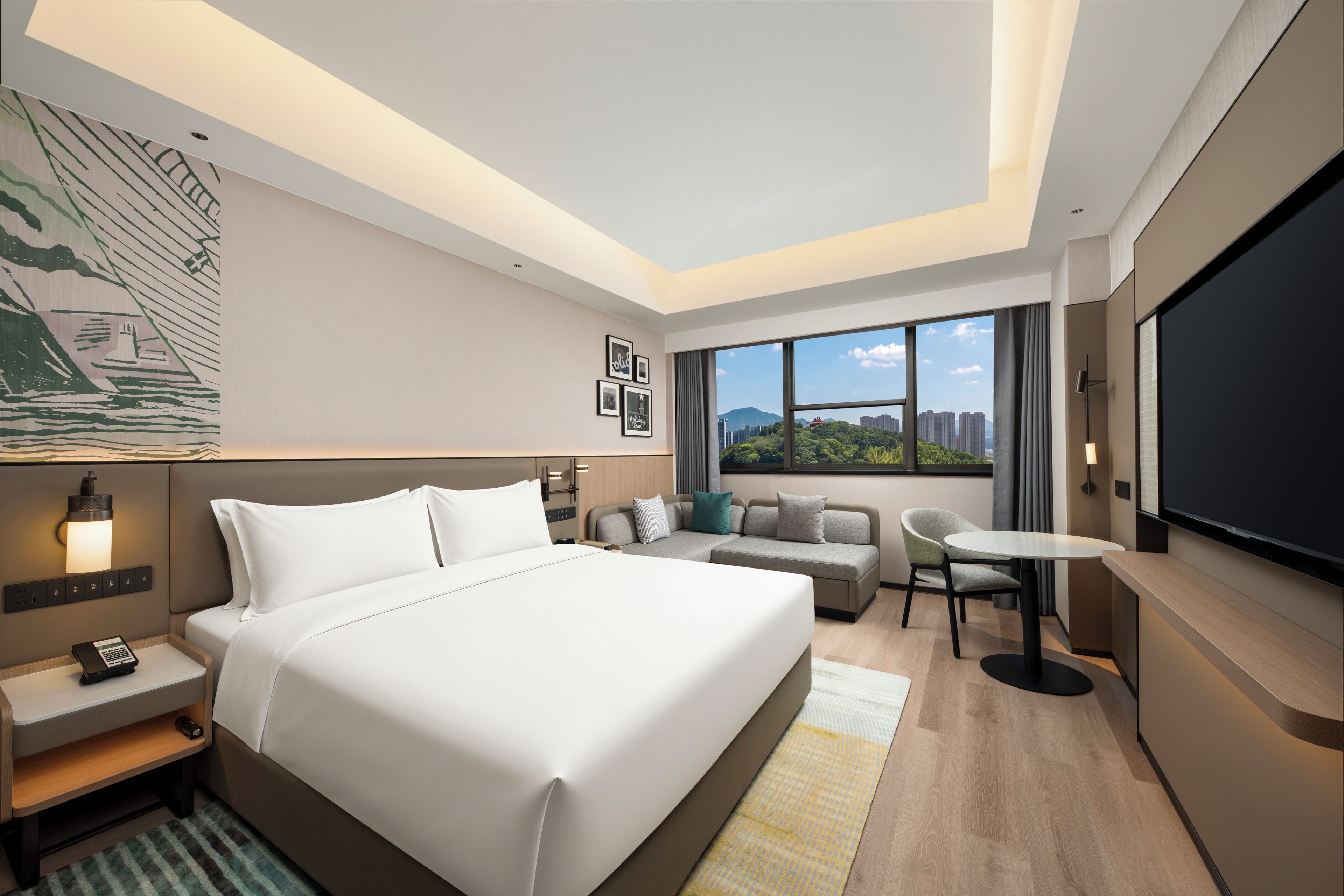 Quarto de hotel moderno com uma cama grande, um sofá, uma mesa pequena, televisão e vista para a cidade.