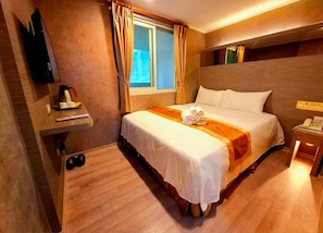 Quarto de hotel com cama, mesa de cabeceira com telefone, pequena mesa com cafeteira e janela com cortinas.