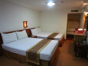 Quarto de hotel com duas camas de solteiro, mesa de cabeceira com abajur, guarda-roupa e pequena escrivaninha com telefone.