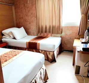 Quarto de hotel com duas camas, uma mesa de escritório com um computador e uma janela com cortinas.