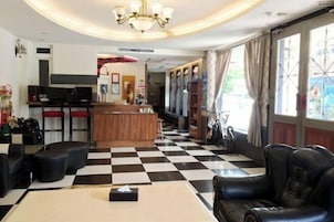 Um saguão de hotel com piso xadrez, balcão de recepção, área de bar e assentos de couro.