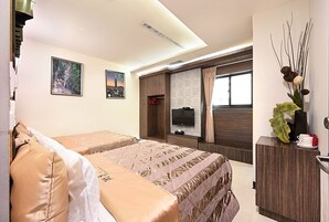 Quarto de hotel com duas camas, televisão, secretária com um vaso e obras de arte nas paredes.