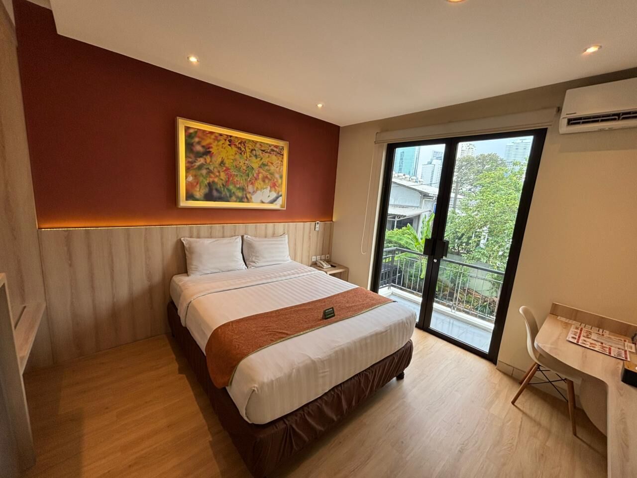 Quarto com cama, mesa de cabeceira, escrivaninha e janela com vista para o verde.