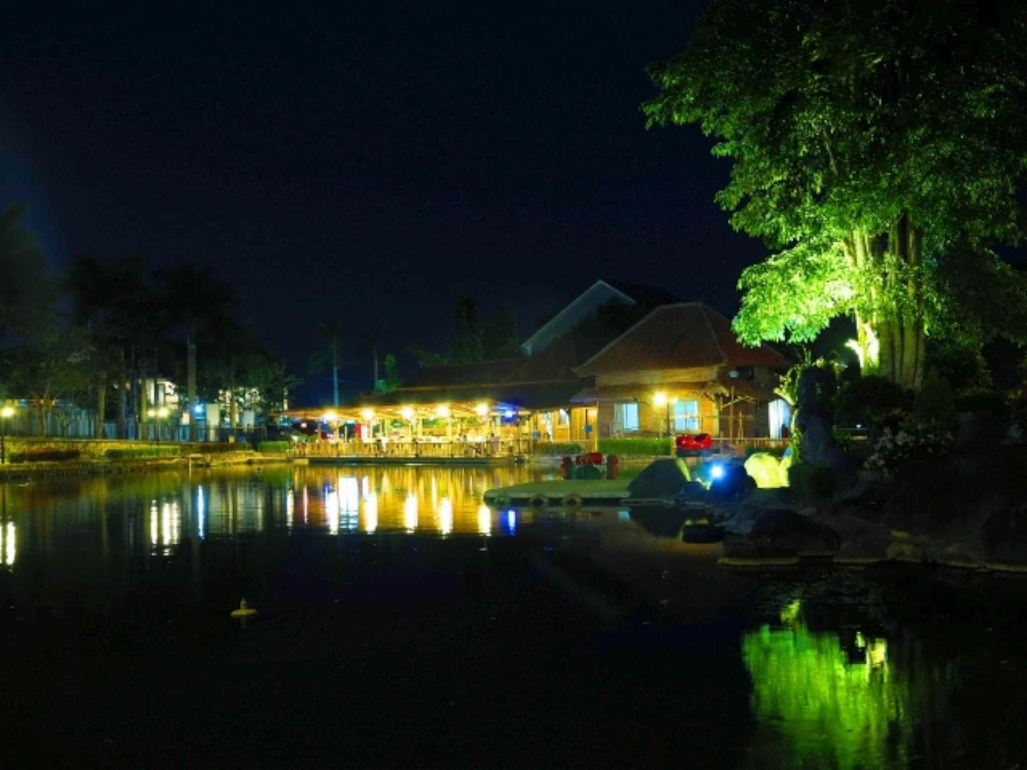 Vista noturna de uma área à beira-lago, com edifícios, um píer e barcos.