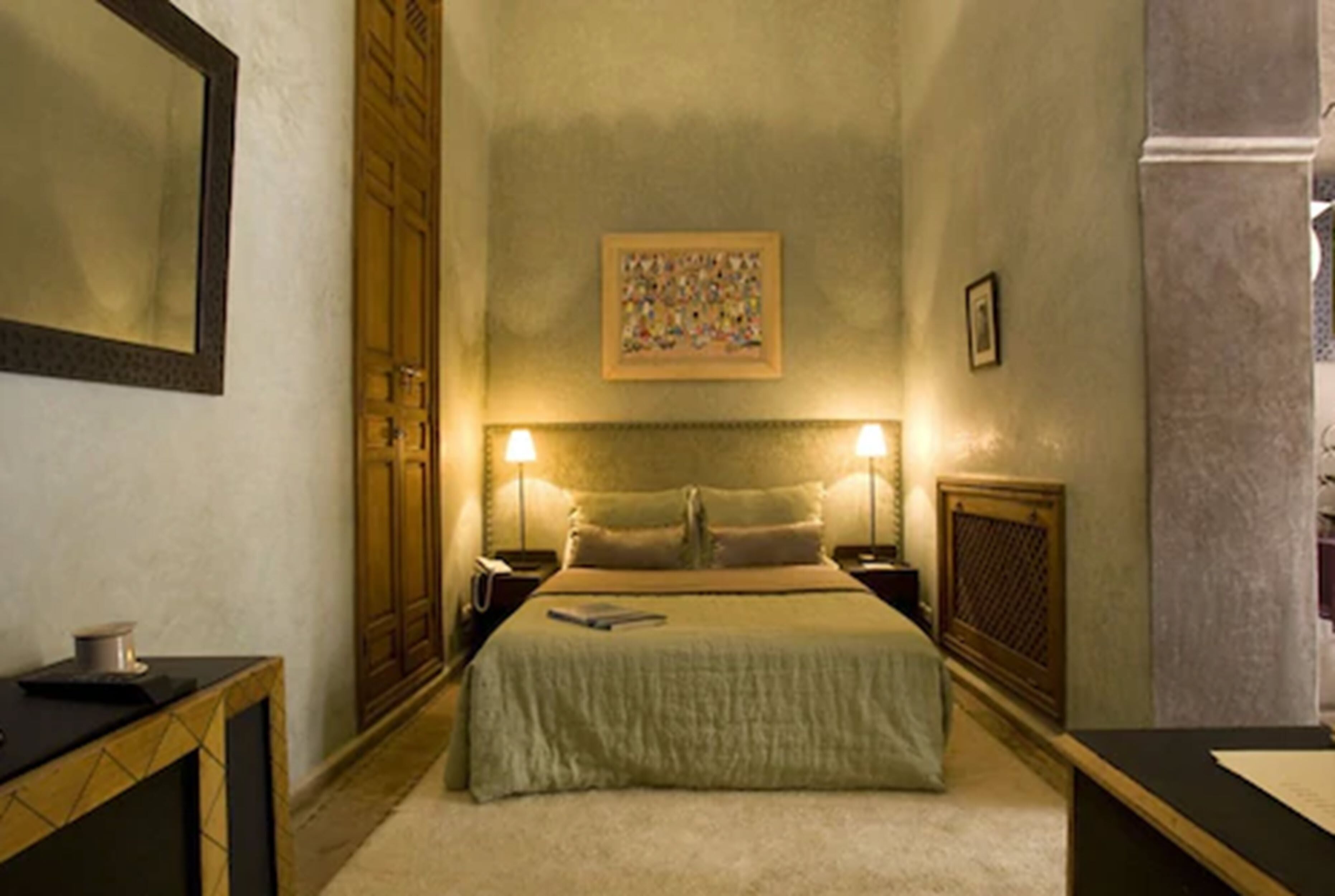 Quarto com uma cama grande, duas luminárias de cabeceira, uma mesinha de cabeceira, um quadro emoldurado na parede e um guarda-roupa de madeira.
