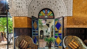 Um interior ornamentado com um grande arco, duas poltronas ricamente decoradas e uma pequena mesa com um vaso.