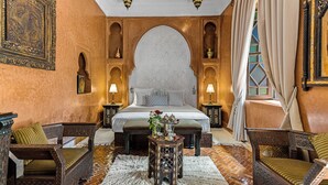 Quarto tradicional marroquino com uma cama grande, mobiliário de madeira ornamentado e um tapete decorativo.