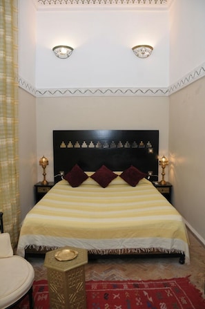 Quarto bem arrumado com cama, mesas de cabeceira e uma cadeira.