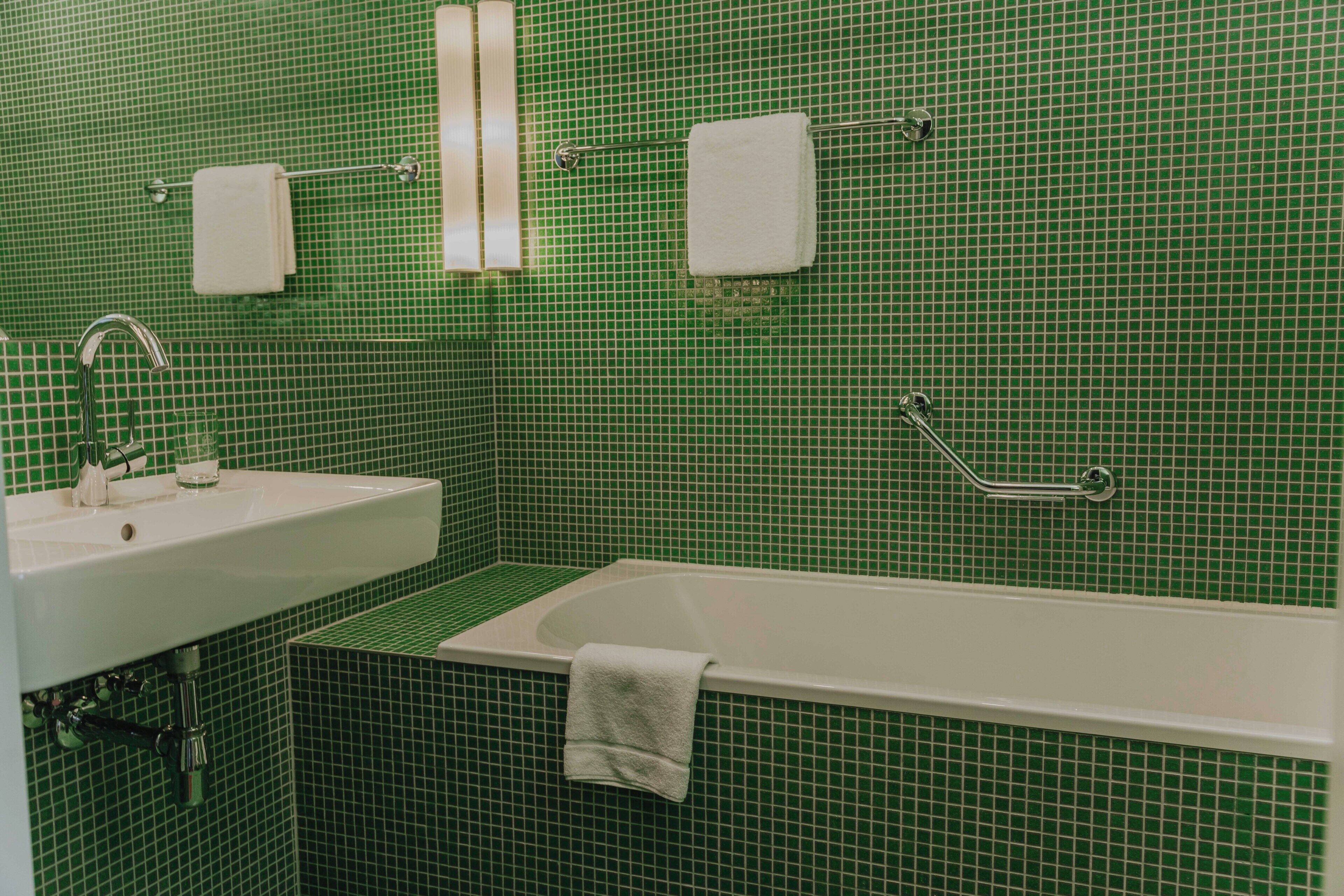 Um banheiro com pia, espelho e banheira, tudo com azulejos verdes.