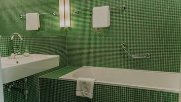 Um banheiro com pia, espelho e banheira, tudo com azulejos verdes.