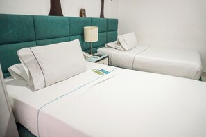 Quarto de hotel com duas camas, cabeceira verde-água, luminária de cabeceira e pequena mesa com telefone e revista.