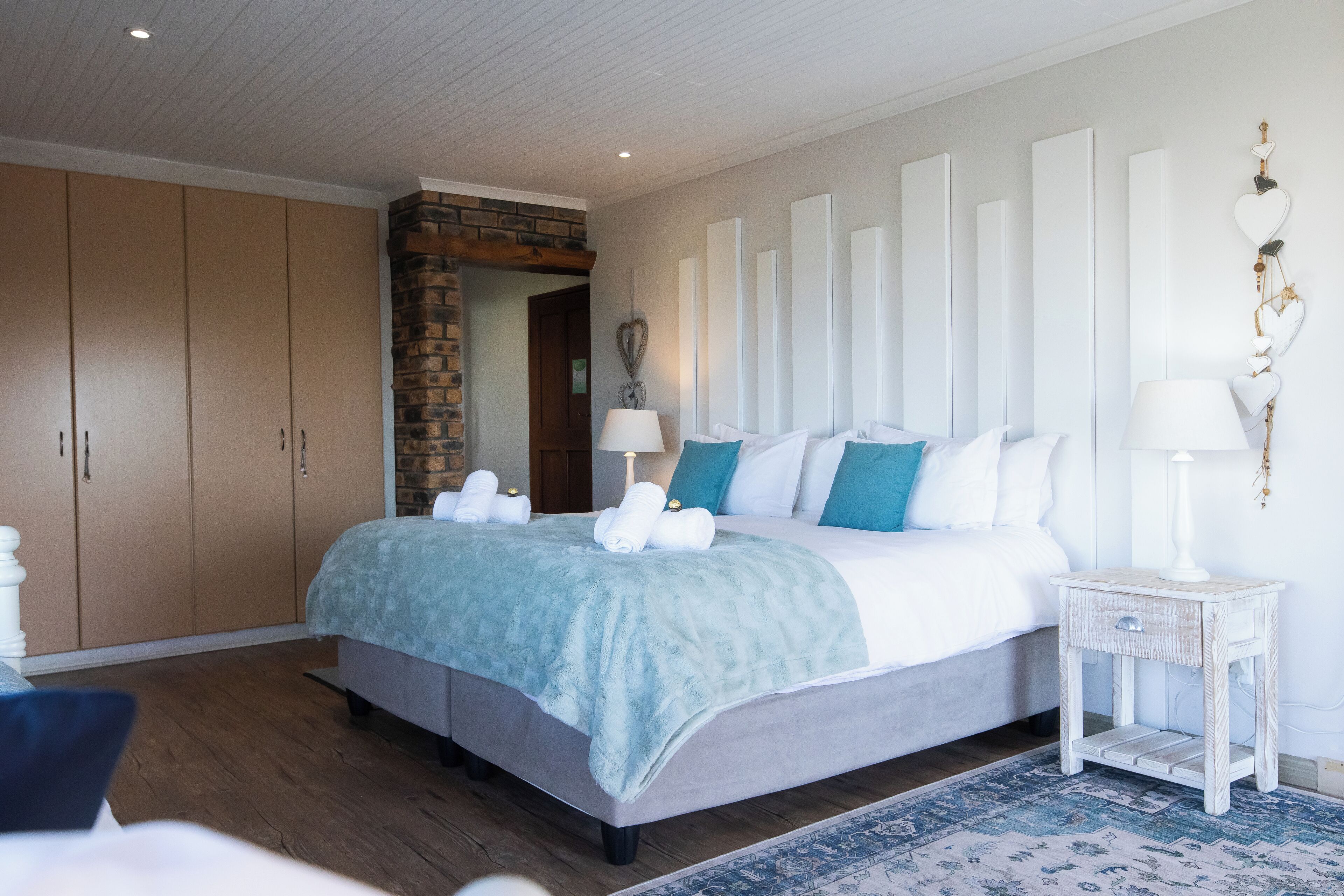 Quarto com cama, mesa de cabeceira, cômoda e parede de destaque em tijolo.