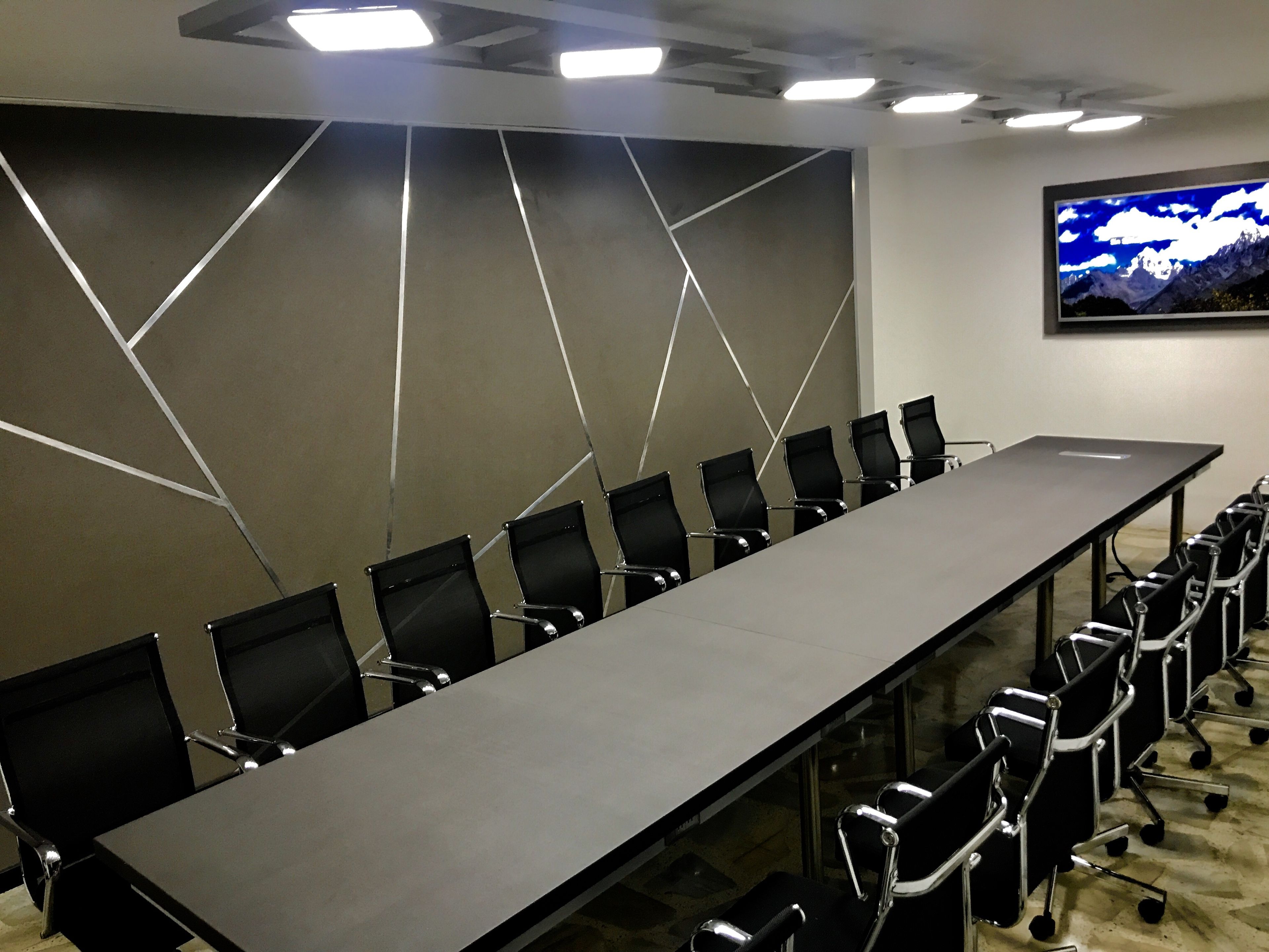 Uma sala de conferências com uma mesa comprida e várias cadeiras, uma tela grande na parede e um design geométrico na parede.