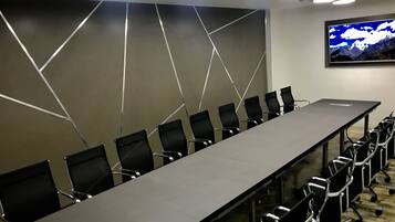 Uma sala de conferências com uma mesa comprida e várias cadeiras, uma tela grande na parede e um design geométrico na parede.