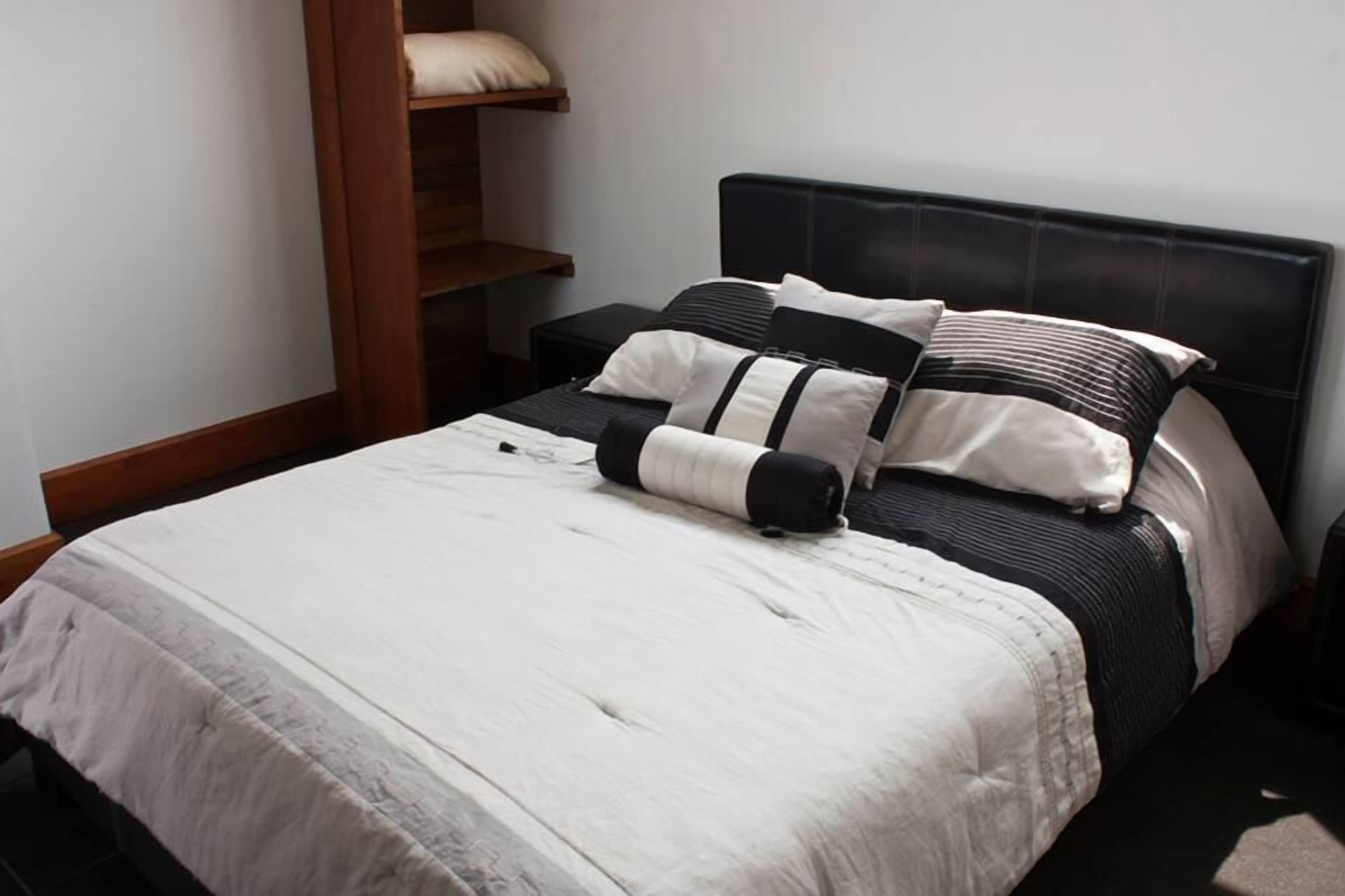 Cama bem arrumada com cabeceira preta, roupa de cama listrada em preto e branco e almofada bege.